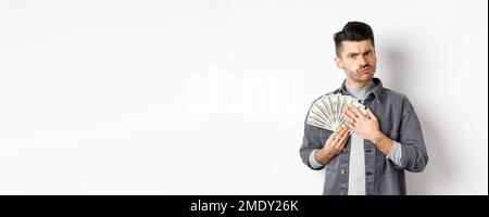 Greedy guy frowning and hugging dollar bills, unwilling to share money ...
