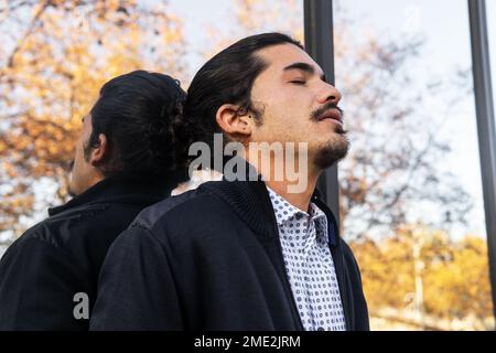 Low angle of calm thoughtful bearded guy in casual clothes standing on ...