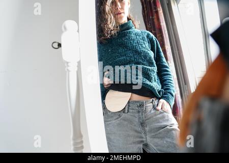 A female colon cancer survivor looking at the ostomy bag in the mirror ...