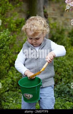 Boy holding bucket and spade standing behind young girl crouched on ...