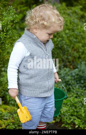 Boy holding bucket and spade standing next to young girl, 2 years 4 ...