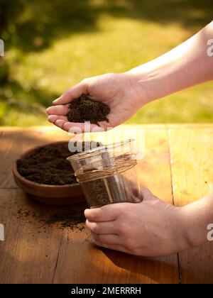 Woman filling pot with soil on wooden table, closeup Stock Photo - Alamy