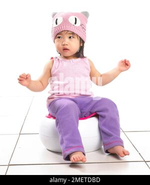 Girl wearing pink vest and pink wool hat, sitting on white potty, 20 months Stock Photo - Alamy