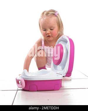 Girl crouching wearing pink vest holding a red potty, 20 months Stock Photo - Alamy