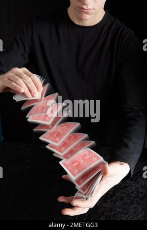 A young man performing a card trick with a deck of red playing cards ...