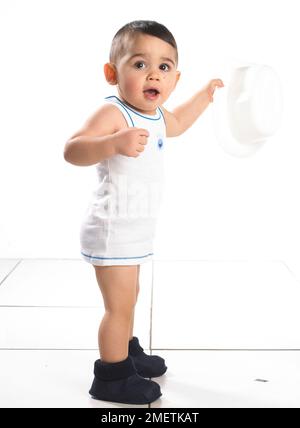 Boy wearing vest and slippers wearing a nappy on his head, 15 months ...
