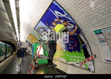 A worker putting up commercial advertising poster on the wall inside of ...