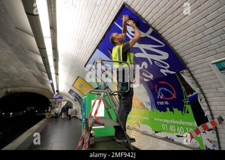 A worker putting up commercial advertising poster on the wall inside of ...