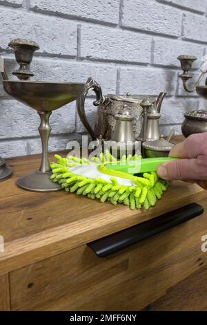 Man dusting wooden cabinet and pewter ornaments with a green microfibre ...