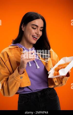 Positive woman holding takeaway sushi and smiling at camera isolated on ...