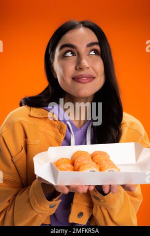Positive woman holding takeaway sushi and smiling at camera isolated on ...