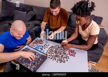 Friends playing jigsaw puzzles at home, on a white wooden table ...