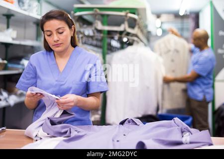 Focused woman dry-cleaning worker checking clean clothes Stock Photo ...