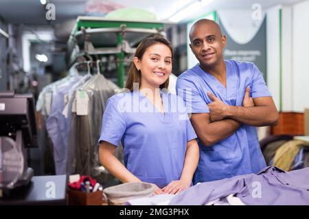 Two workers offering professional dry cleaning, showing clean clothing ...