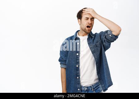 Upset young man slaps his forehead and looks devestated, frustrated by ...