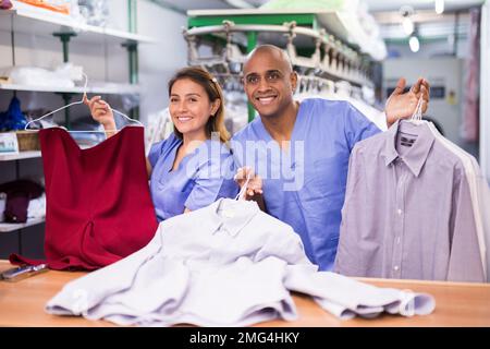 Two workers offering professional dry cleaning, showing clean clothing ...