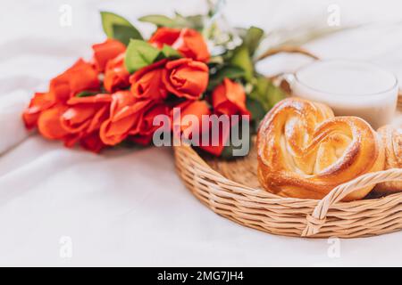 Wicker tray with pastries and coffee and flowers on white bed linen ...