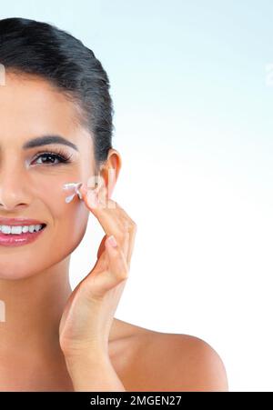 Beautiful woman applying cream onto her face on light green background ...