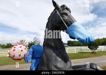 A statue of a horse with a mask, carries a rider in PPE holding a model ...