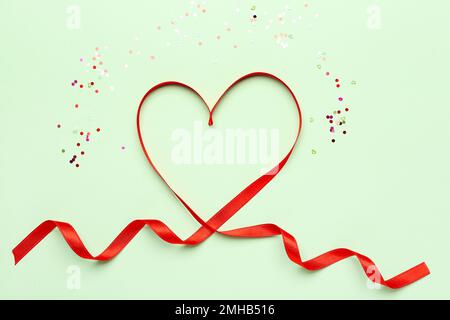 Sequins and heart made of red satin ribbon on green background ...