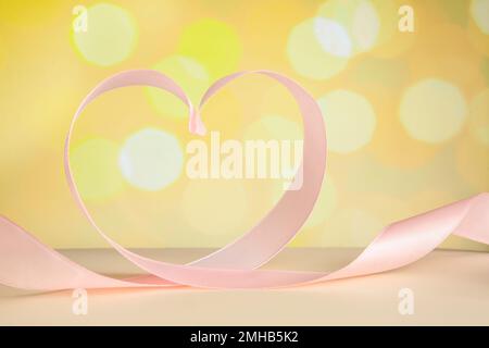 Heart made of pink satin ribbon on table against blurred lights Stock ...
