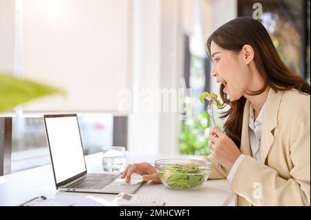 Millennial businesswoman having lunch while looking at computer Stock ...