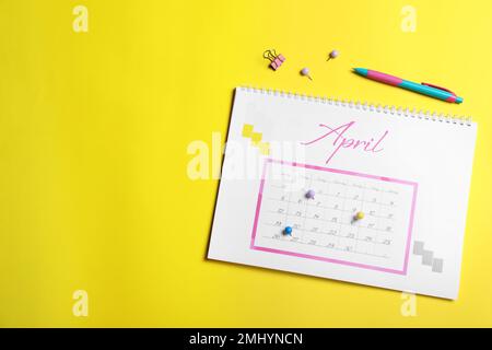 Calendar page marked with drawing pins on yellow background, flat lay ...