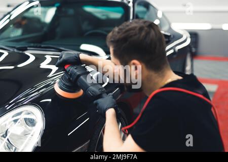 Front view of car detailing process. Specialist using PPF to cover red ...