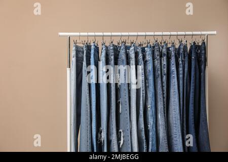 Rack with stylish jeans on beige background, closeup Stock Photo - Alamy
