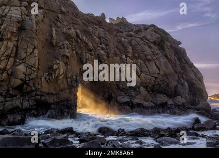 The setting sun shining through Keyhole Arch at Pfeiffer Beach, Big Sur ...