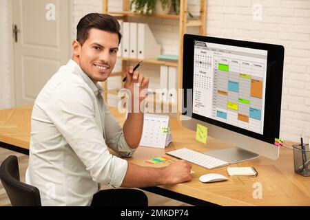 Handsome man using calendar app on computer in office Stock Photo - Alamy