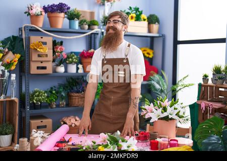 Young redhead man florist smiling confident using laptop at flower shop ...