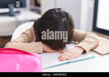 Adorable hispanic girl student stressed leaning on book at classroom ...