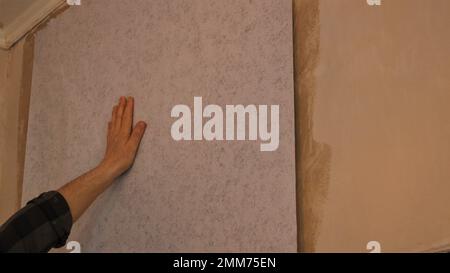 man pasting a strip of gray wallpaper on the room wall next to the ...