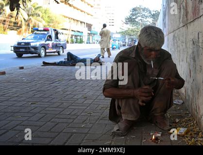 A Pakistani drug addict smokes heroin on a roadside in Karachi ...