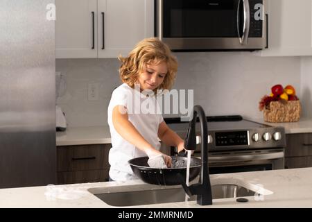 Child housekeeper washing the dishes on soapy water. Cute Funny boy ...