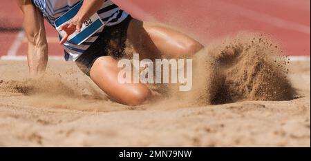 Female athlete long jump landing sand spray, landing in long jump in ...