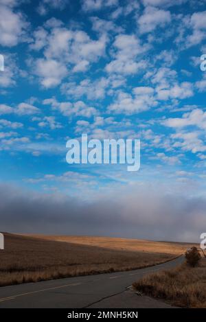 Sun beam across a prairie hillside, blue sky dotted with white clouds ...