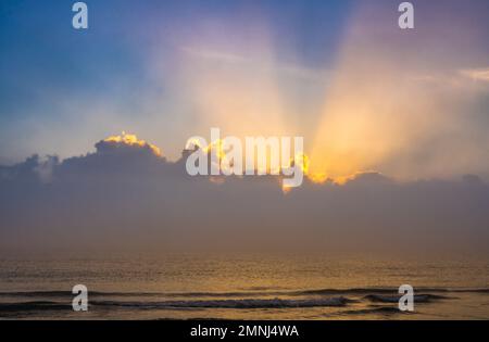 Sun rising above calm ocean Stock Photo - Alamy