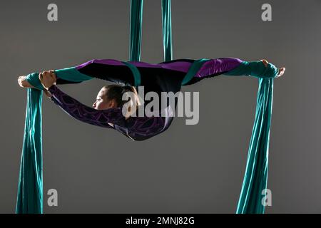 Aerial performer doing splits on chains in dramatic lighting with red ...