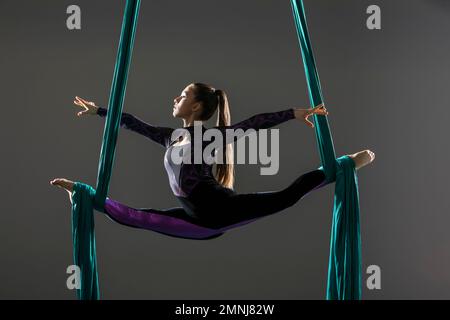 Aerial performer doing splits on chains in dramatic lighting with red ...