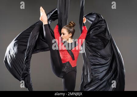 Aerial performer doing splits on chains in dramatic lighting with red ...