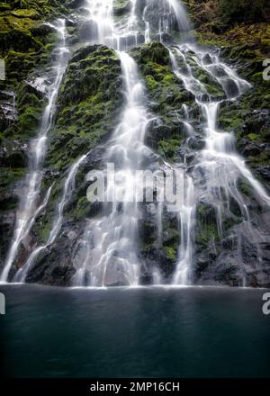 A small waterfall running down a moss covered stone wall Stock Photo ...