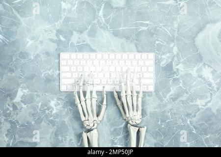 Human skeleton using computer keyboard at grey marble table, top view ...