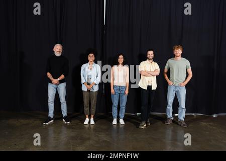 full length of happy multiethnic actors holding hands and bowing on ...