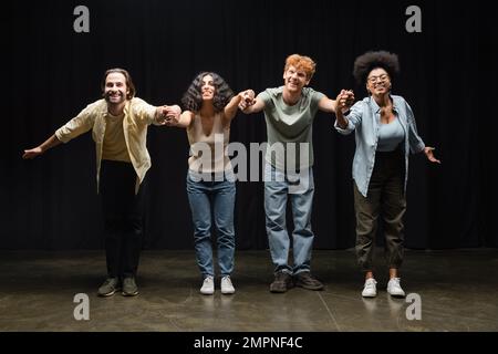 full length of happy multiethnic actors standing with raised hands on ...
