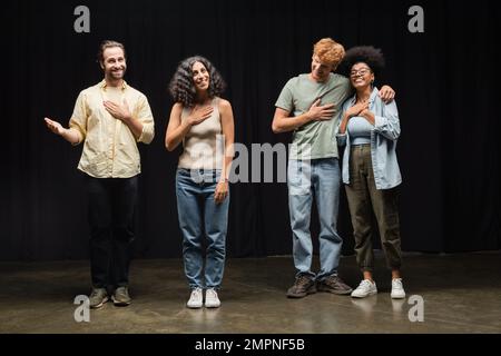 full length of happy multiethnic actors standing with raised hands on ...