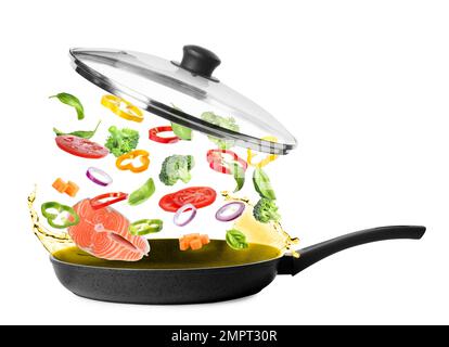Many different ingredients falling into frying pan on white background ...