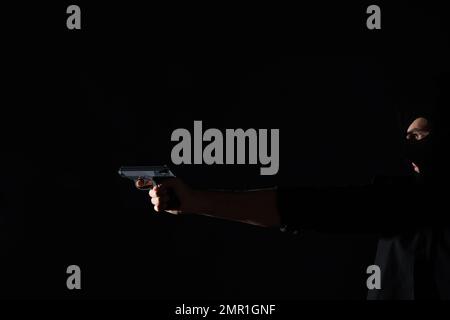 Professional killer with gun on black background, closeup. Space for ...