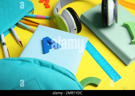 Yellow backpack with school stationery and headphones on bench in park ...